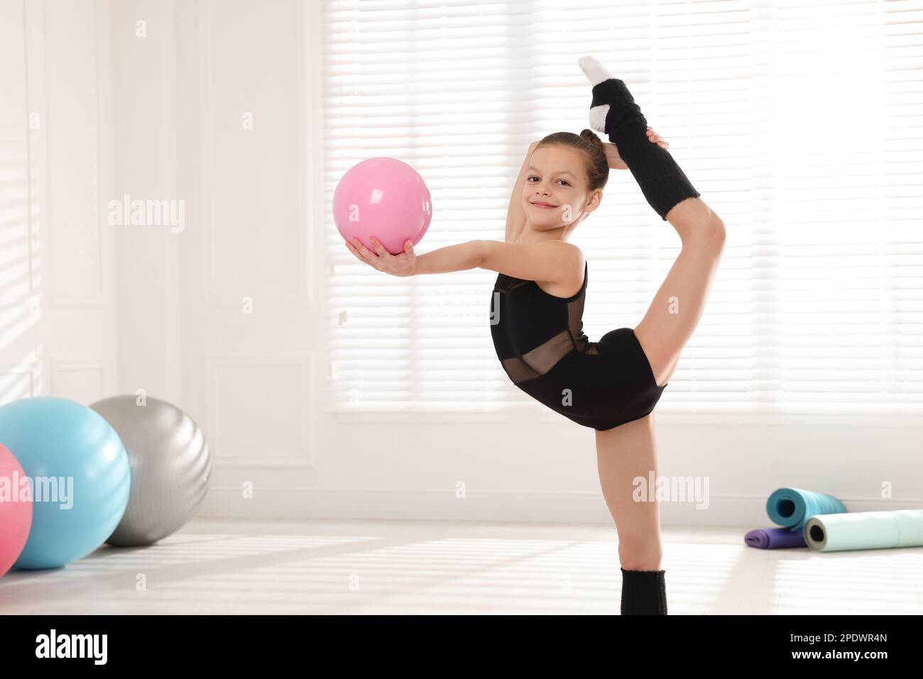 Cute little gymnast with ball doing standing split indoors Stock Photo ...