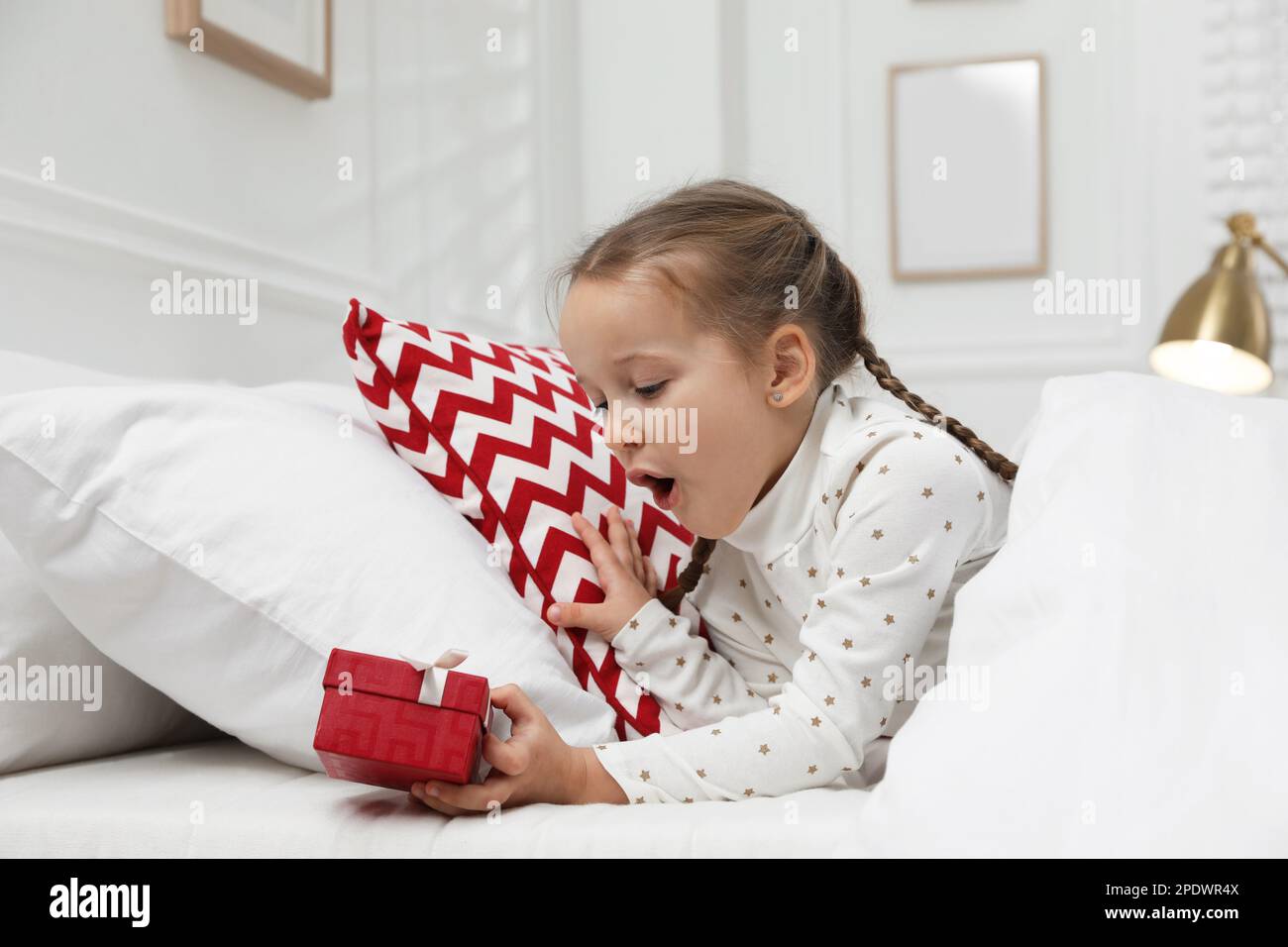 Excited little girl finding gift box under pillow in bed at home. Saint ...