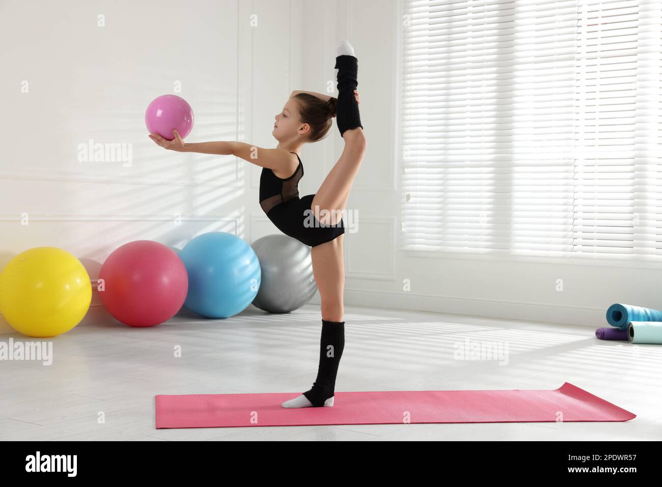 Cute little gymnast with ball doing standing split indoors Stock Photo ...