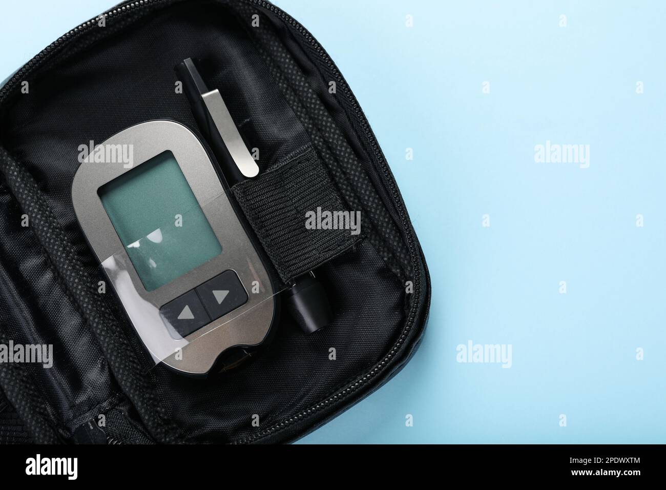 Digital glucometer and lancet pen in bag on light blue background, top ...