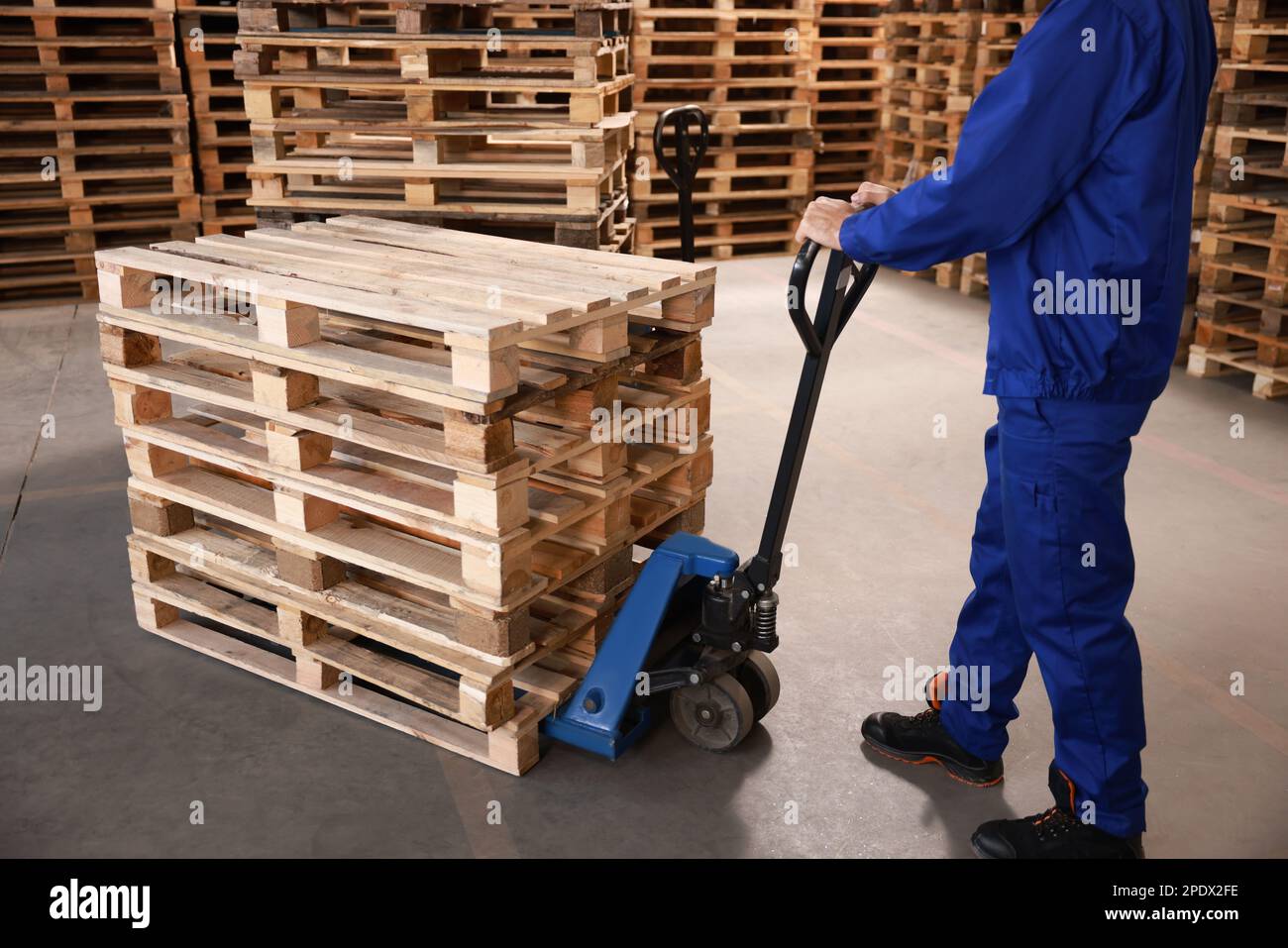 Worker moving wooden pallets with manual forklift in warehouse, closeup ...