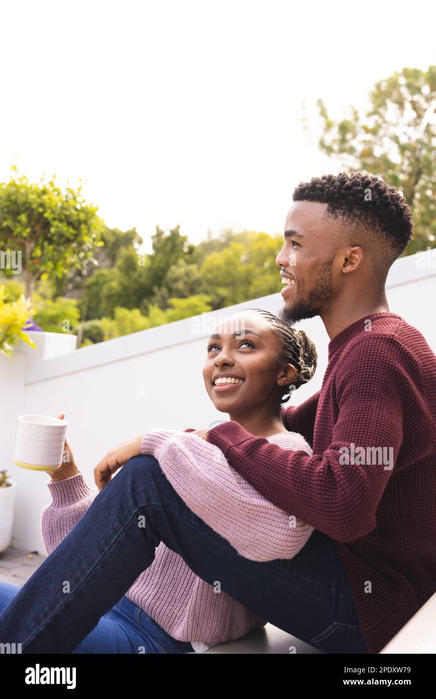 Happy african american couple sitting on stairs in garden, drinking ...