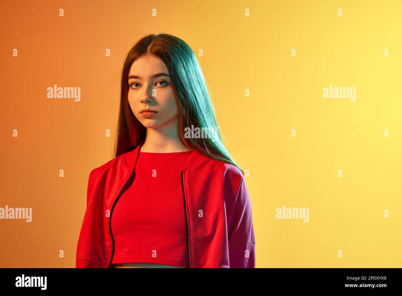Emotionless young girl with long hair looking at camera over orange ...