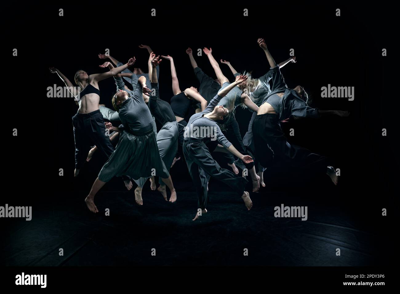 Flying high. Group of young artistic people making freestyle performance, dancing against black ...