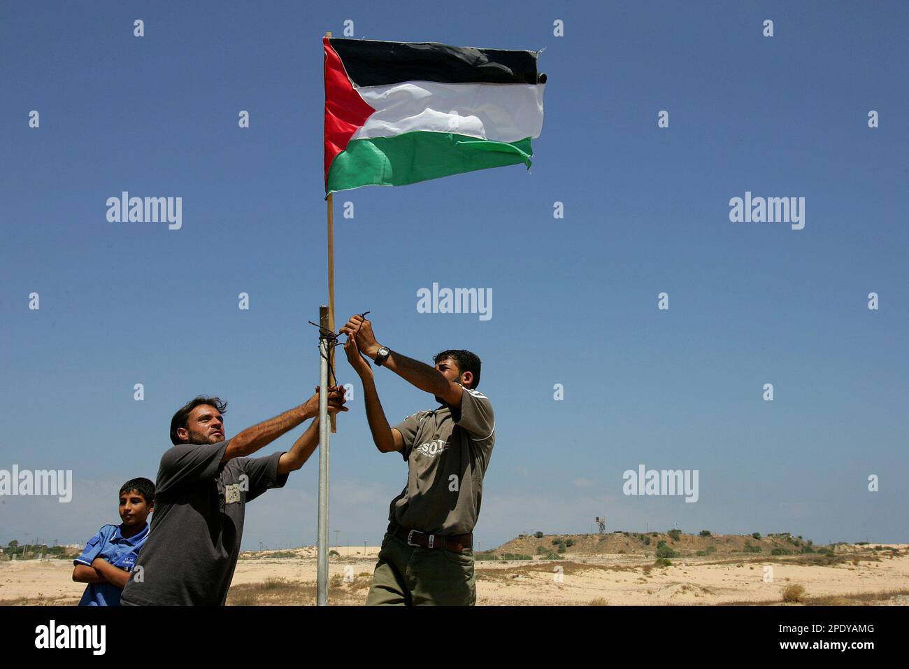 Palestinian men secure a Palestinain flag to a pole, with an Israeli ...