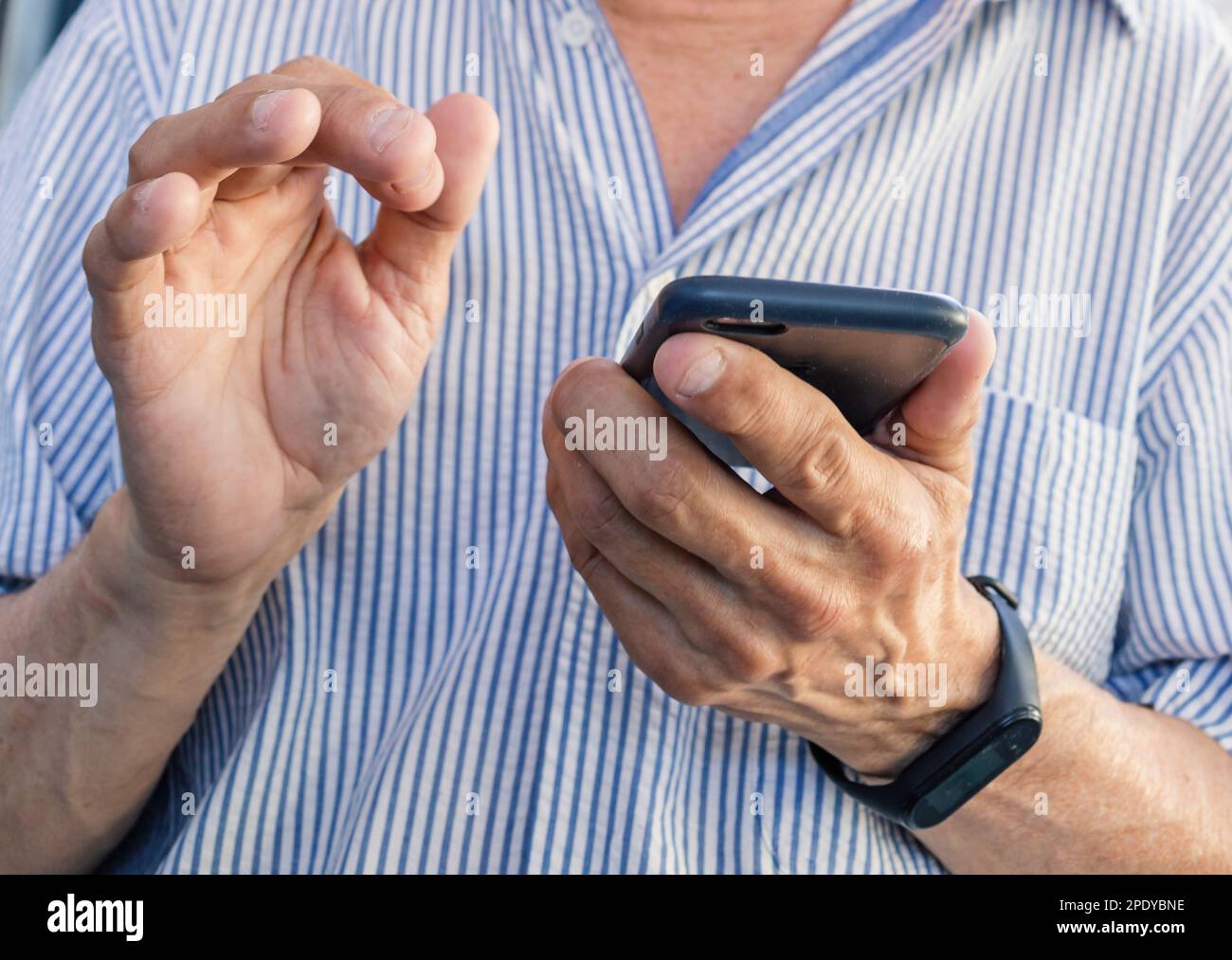 An elderly man holds a mobile phone in his hands with nibbled nails ...