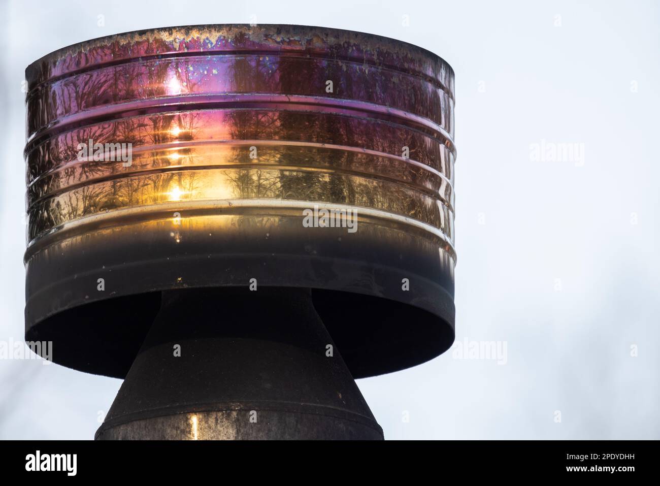 Round shiny metal chimney with heat tint and soot is under blue sky on ...