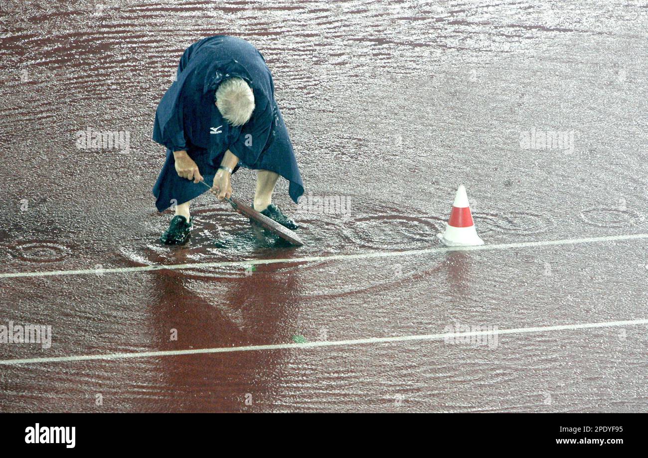 An official opens a drain near the track as rain pours on the Olympic ...