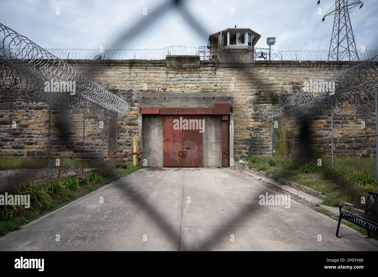 A dimly lit prison cell with a metal door in the foreground, giving a ...