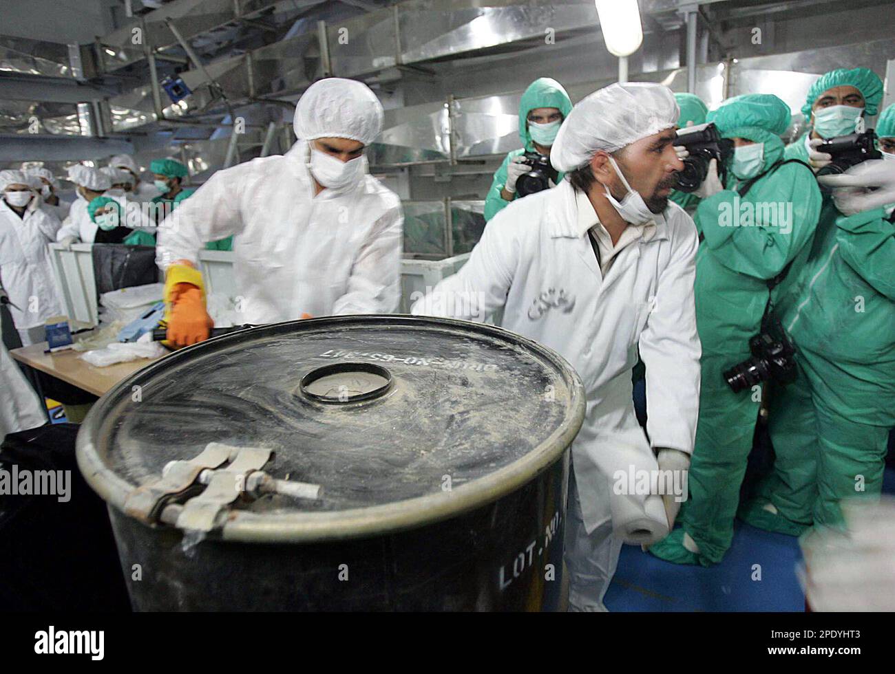 Two technicians carry a box containig uranium ore concentrate, known as ...