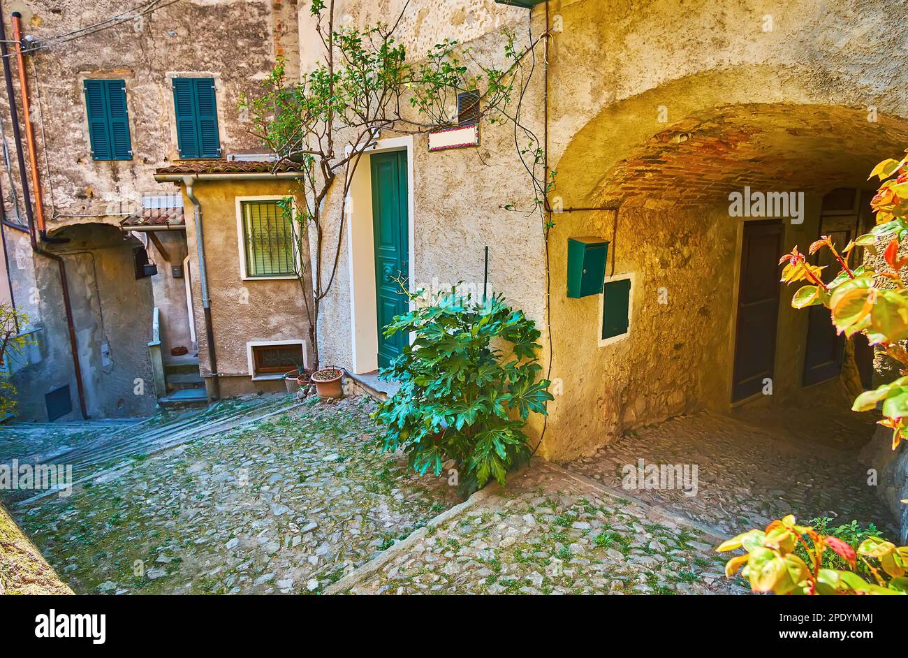 The old stone street with green plants in pots and arched passes with ...