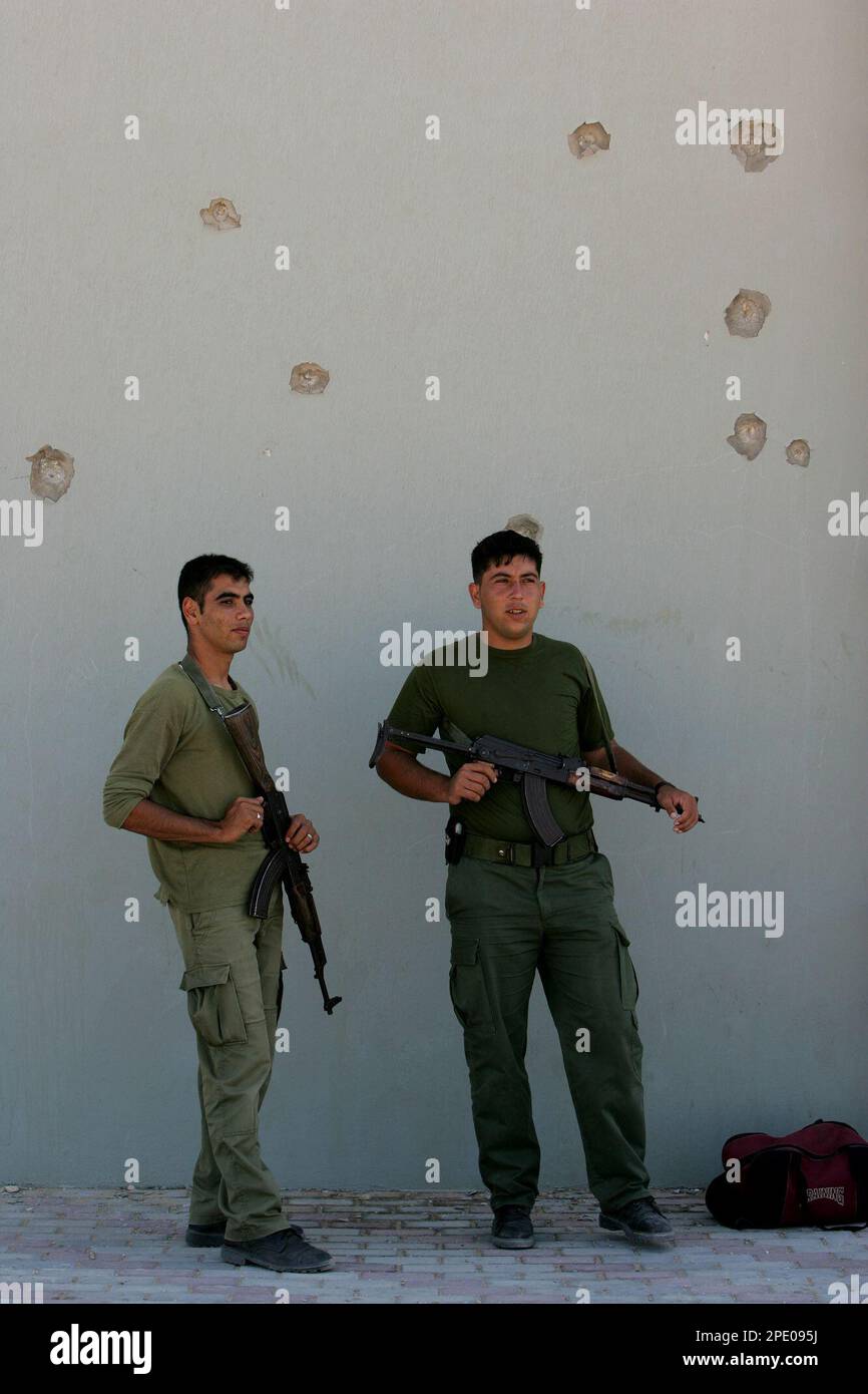 Palestinian security officer stand in front of a bullet-ridden wall ...