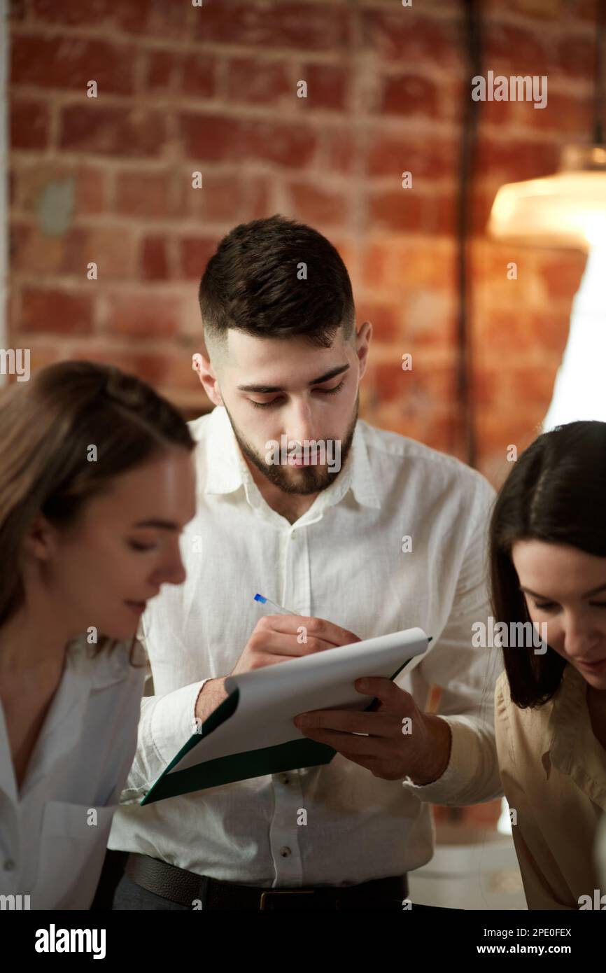 Young man, team leader in official clothes at business meeting with colleagues at office ...