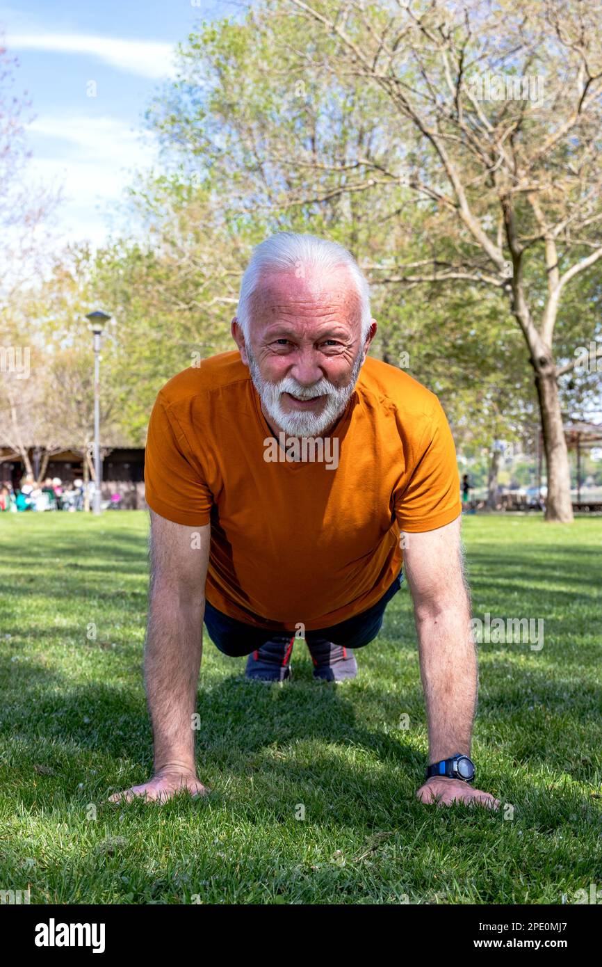 Portrait of a senior man exercising, doing push ups in the park. An ...