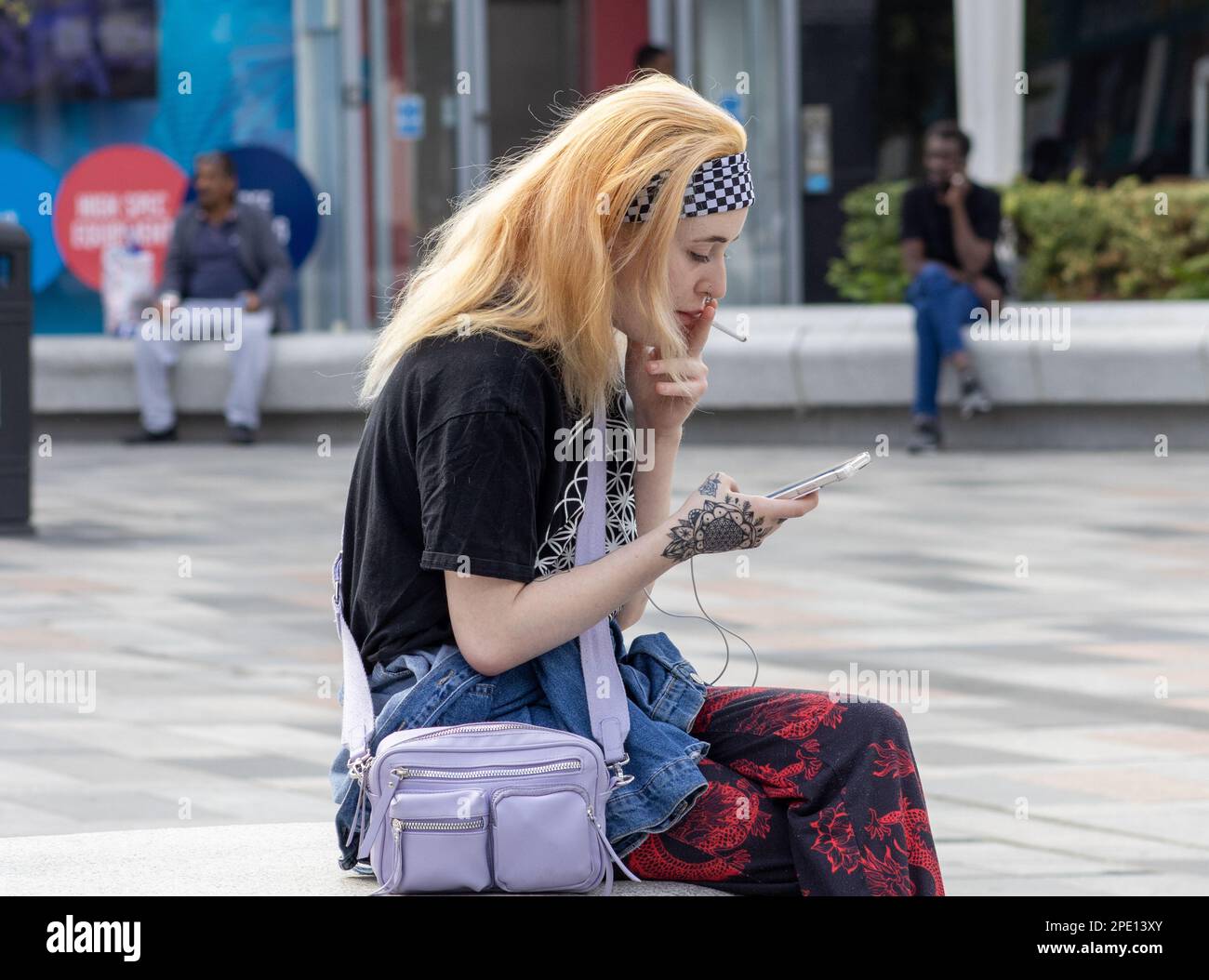 Young woman looking at her phone whilsrt smoking Stock Photo - Alamy