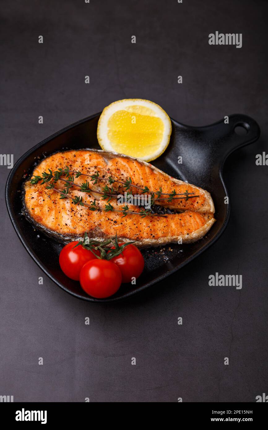 Grilled salmon with cherry tomatoes, thyme and lemon on a small black ...
