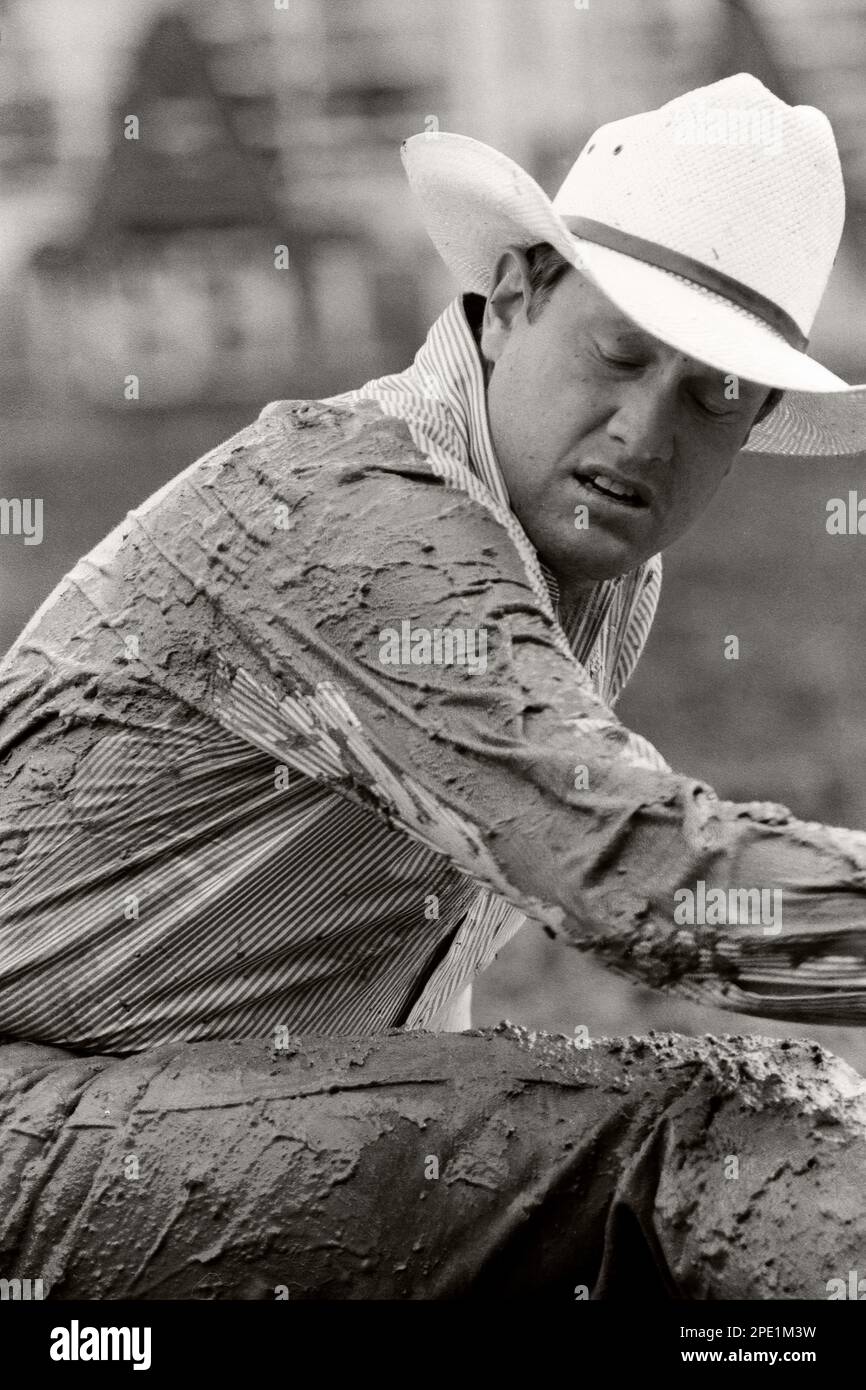 A rodeo cowboy covered in mud after being thrown off a bucking stock ...
