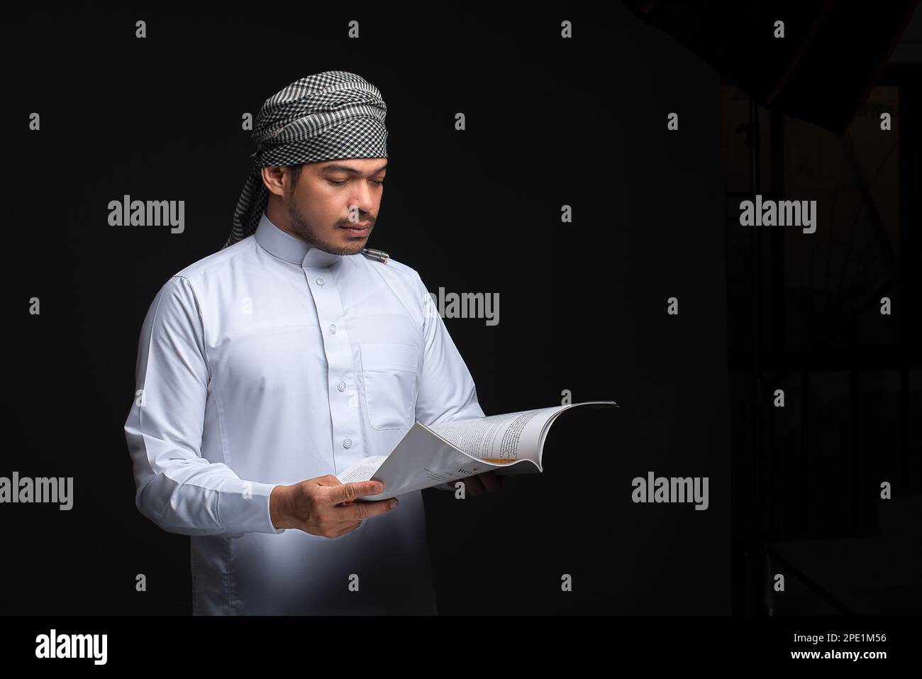 A Muslim male in a traditional headdress and outfit posing with a book ...