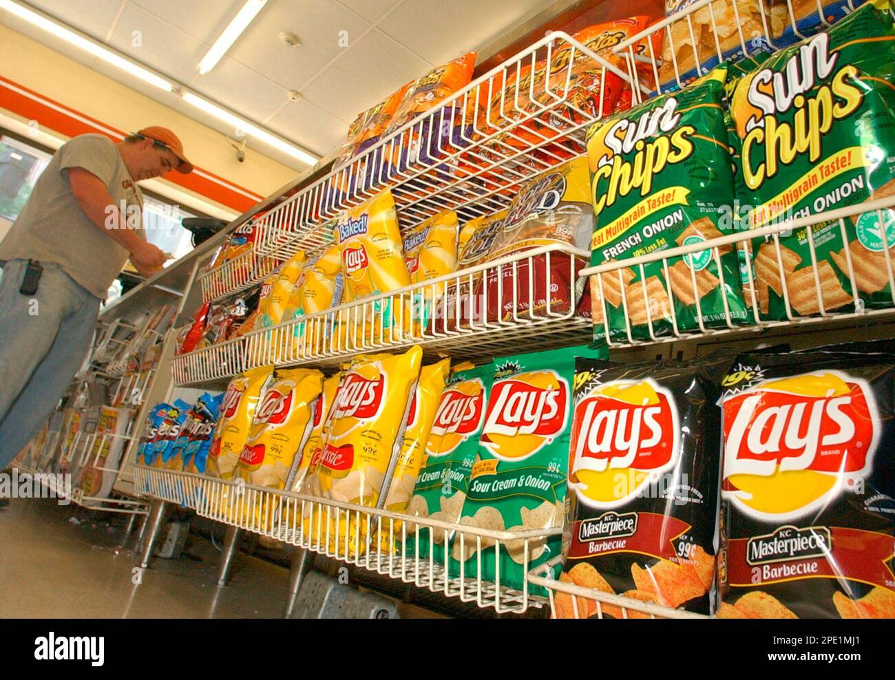 A convienence store customer make a purchase next to a shelf of Frito ...