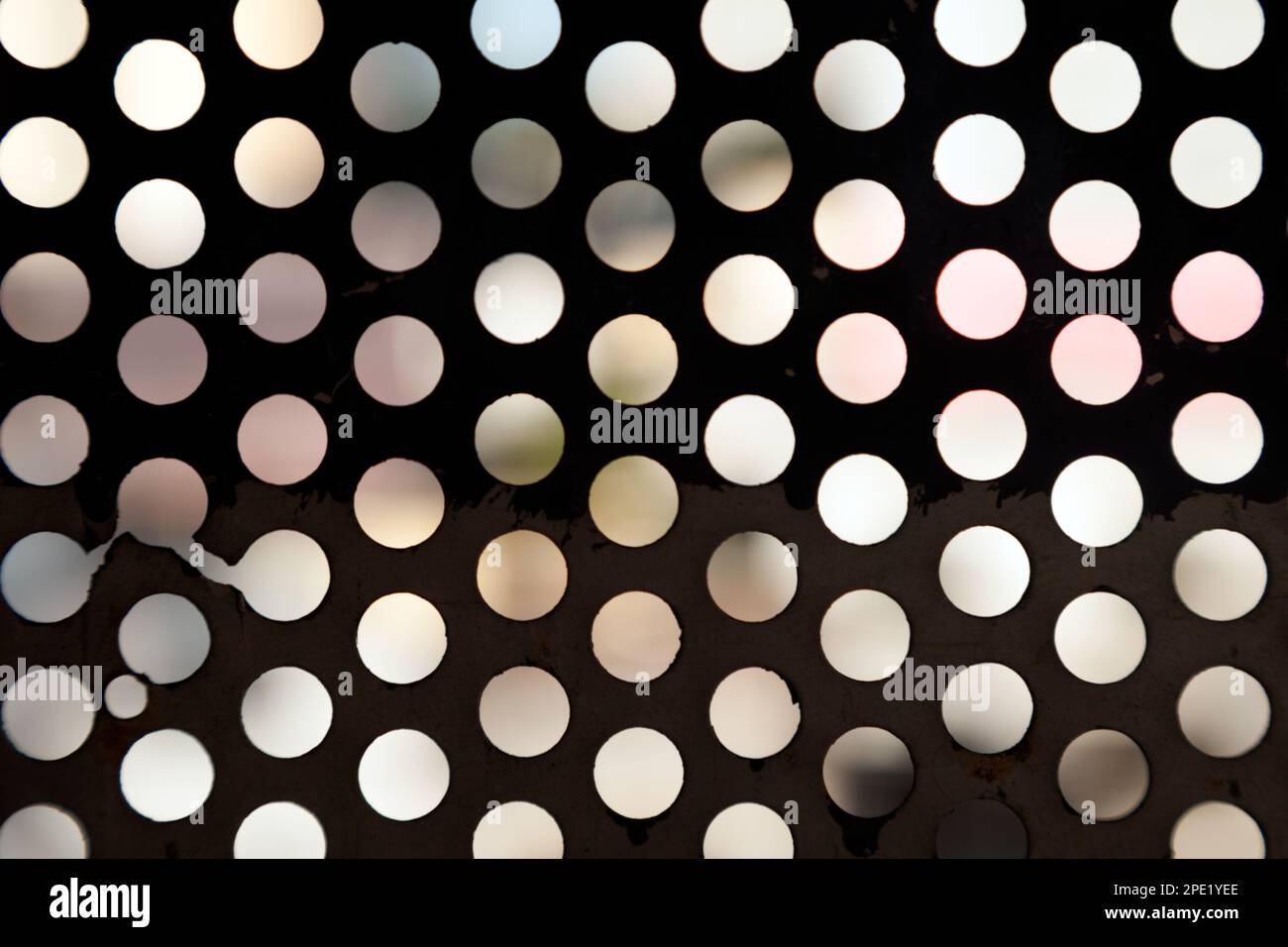 Light coming from outside through round holes in an old black metal ...