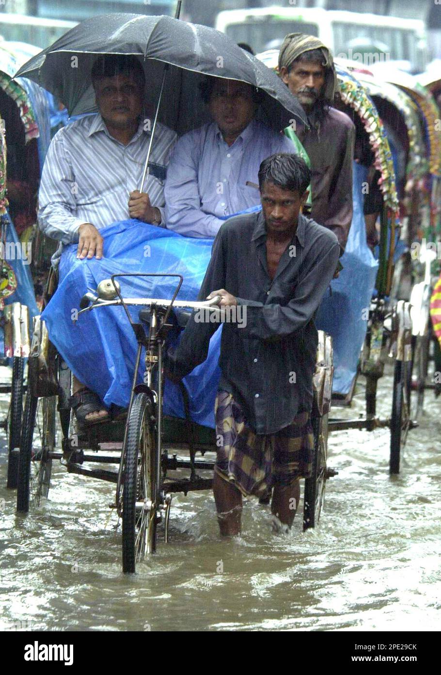Cycle rickshaw pullers take customers through rain at the Motijeel area ...