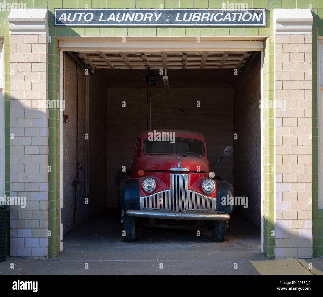 An aged red pickup truck is parked in a garage beneath a sign, clearly ...
