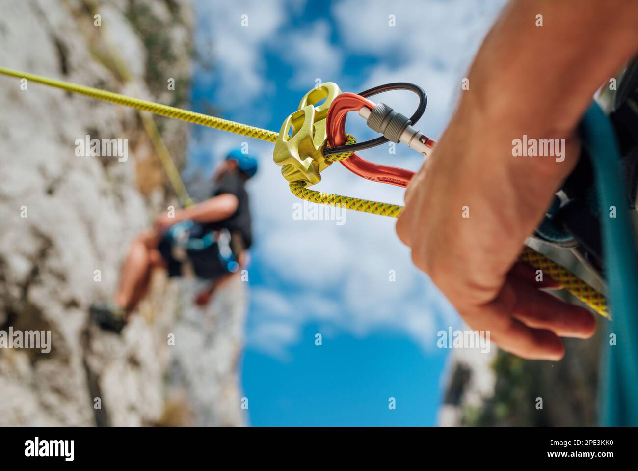 Belay device close-up shot with a boy on the cliff climbing wall. He ...