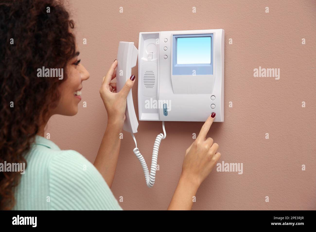 Young African-American woman pressing button on intercom panel indoors ...
