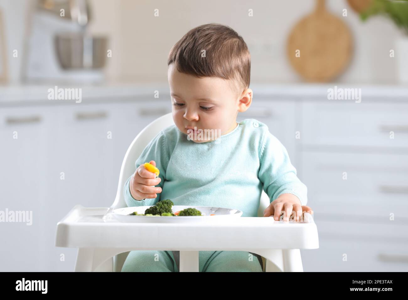 Cute little baby eating healthy food in high chair at home Stock Photo ...