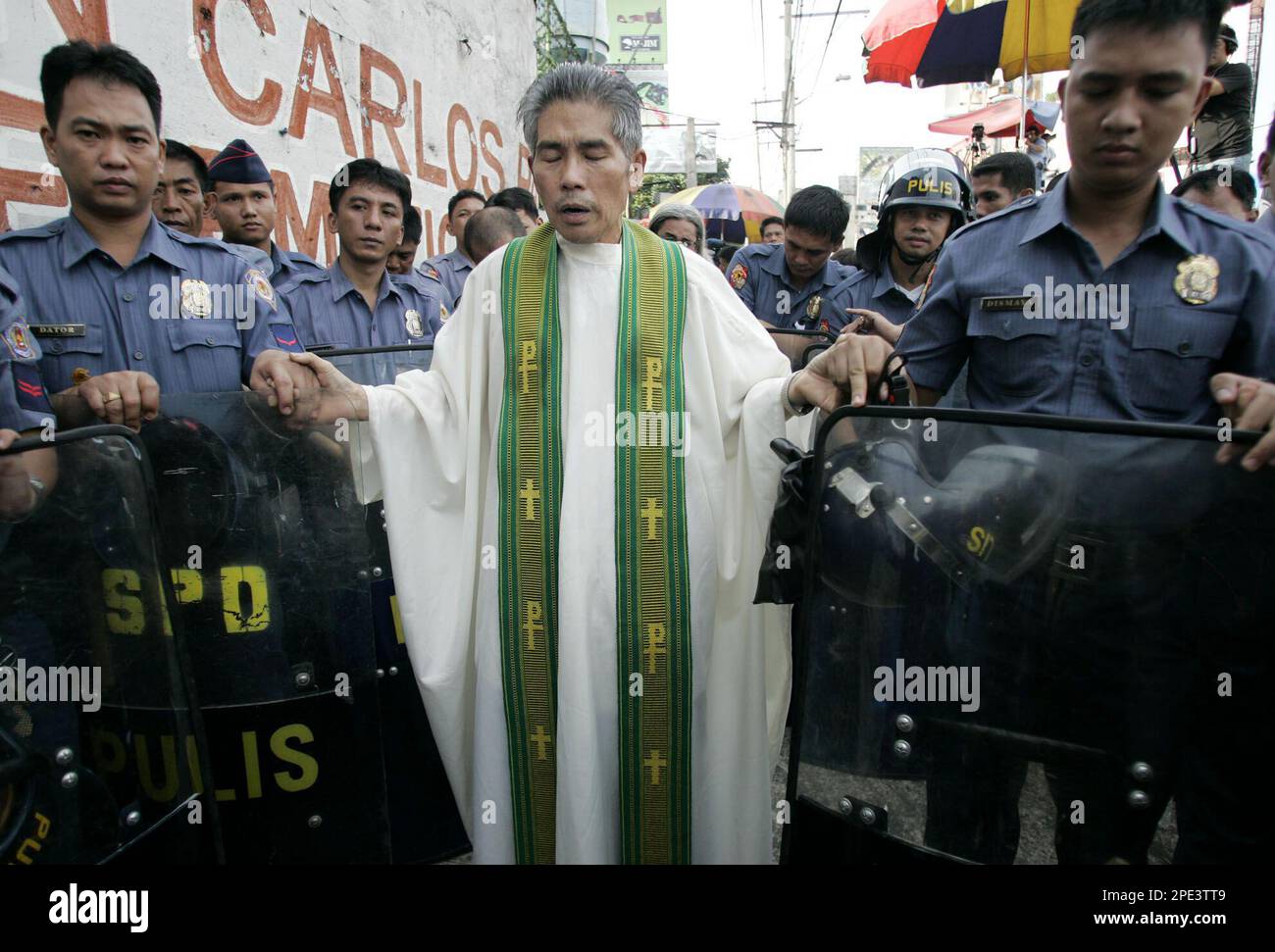 Filipino catholic priest Joe Dizon, center, holds hands with anti-riot policemen as he conducts ...
