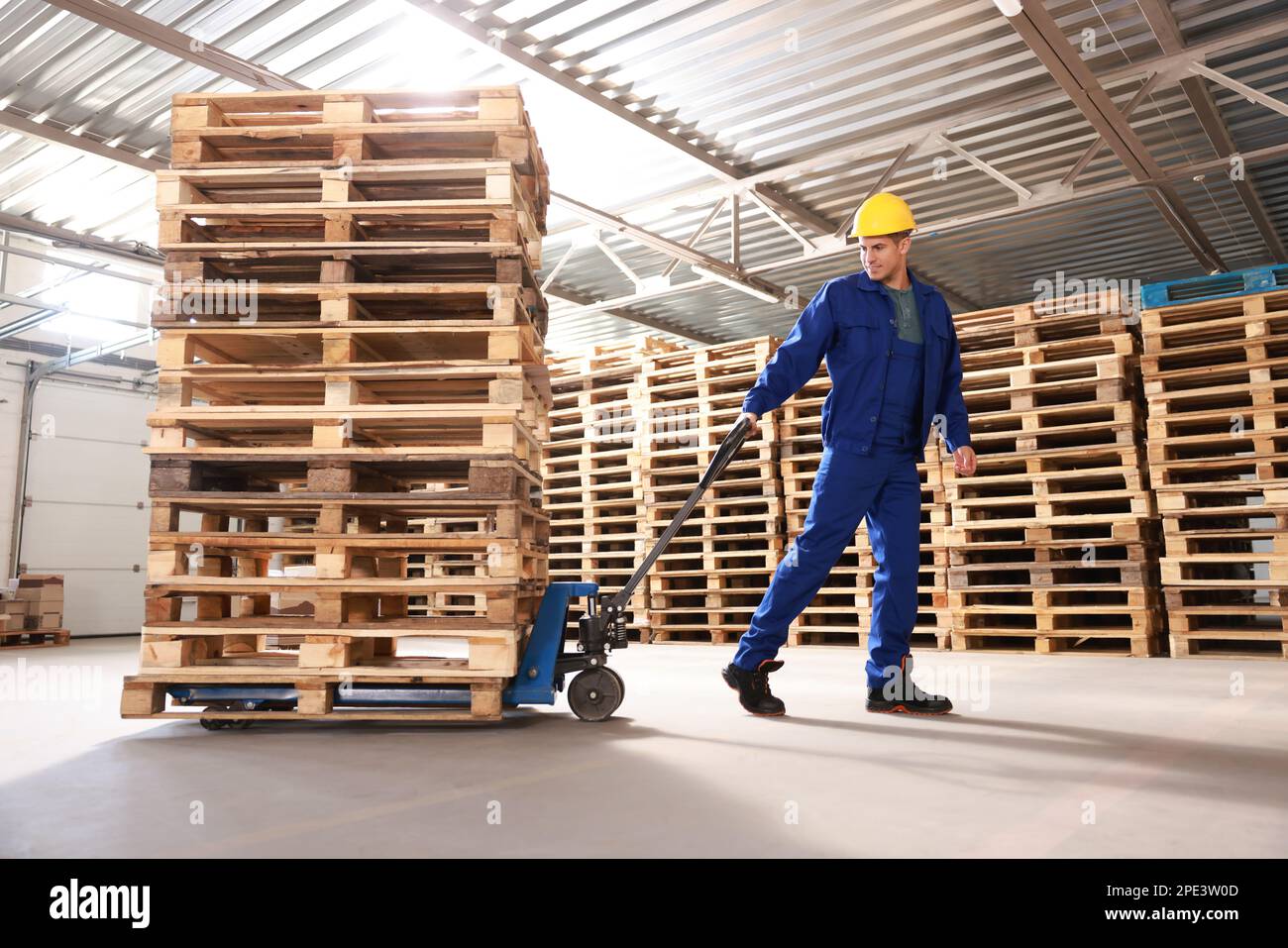 Worker moving wooden pallets with manual forklift in warehouse Stock ...