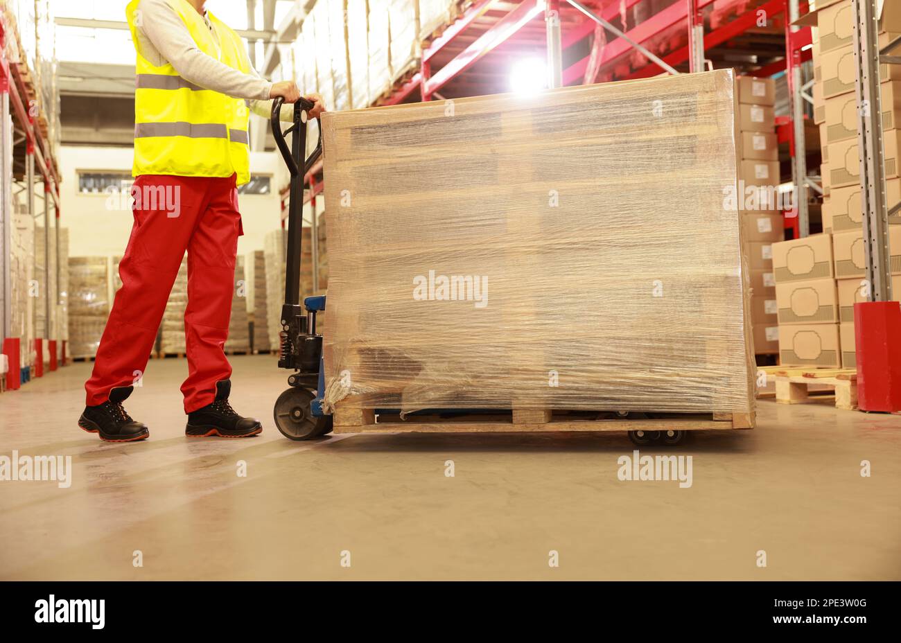 Worker moving wrapped wooden pallets with manual forklift in warehouse ...