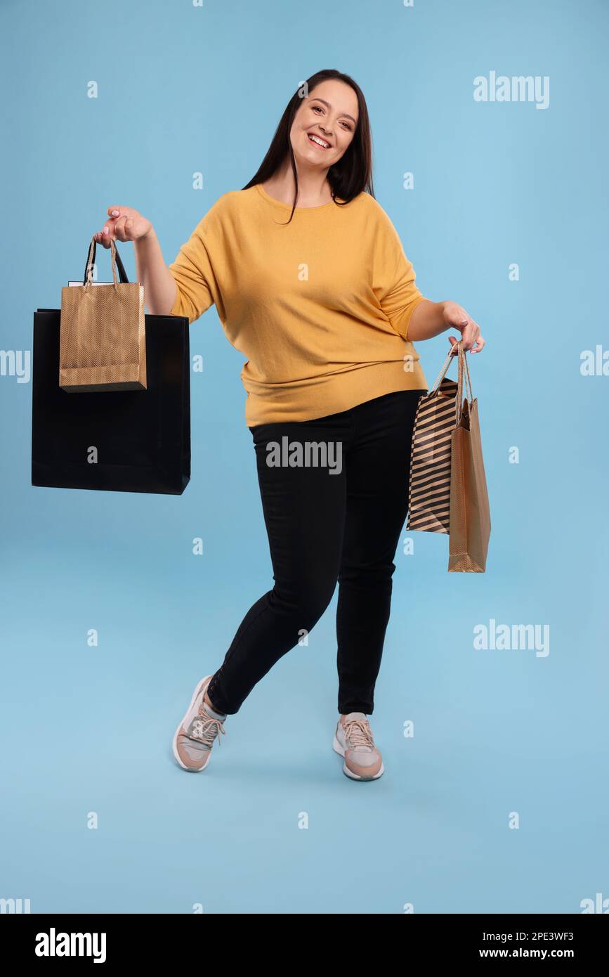 Beautiful overweight woman with shopping bags on turquoise background ...