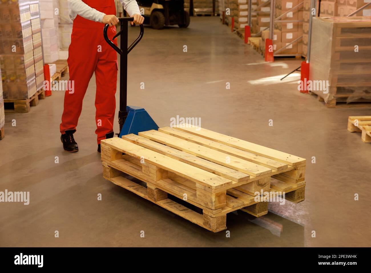 Worker moving wooden pallets with manual forklift in warehouse, closeup ...