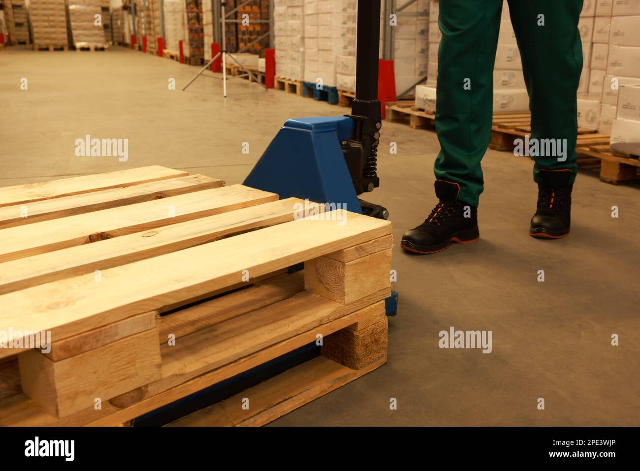Worker moving wooden pallets with manual forklift in warehouse, closeup ...