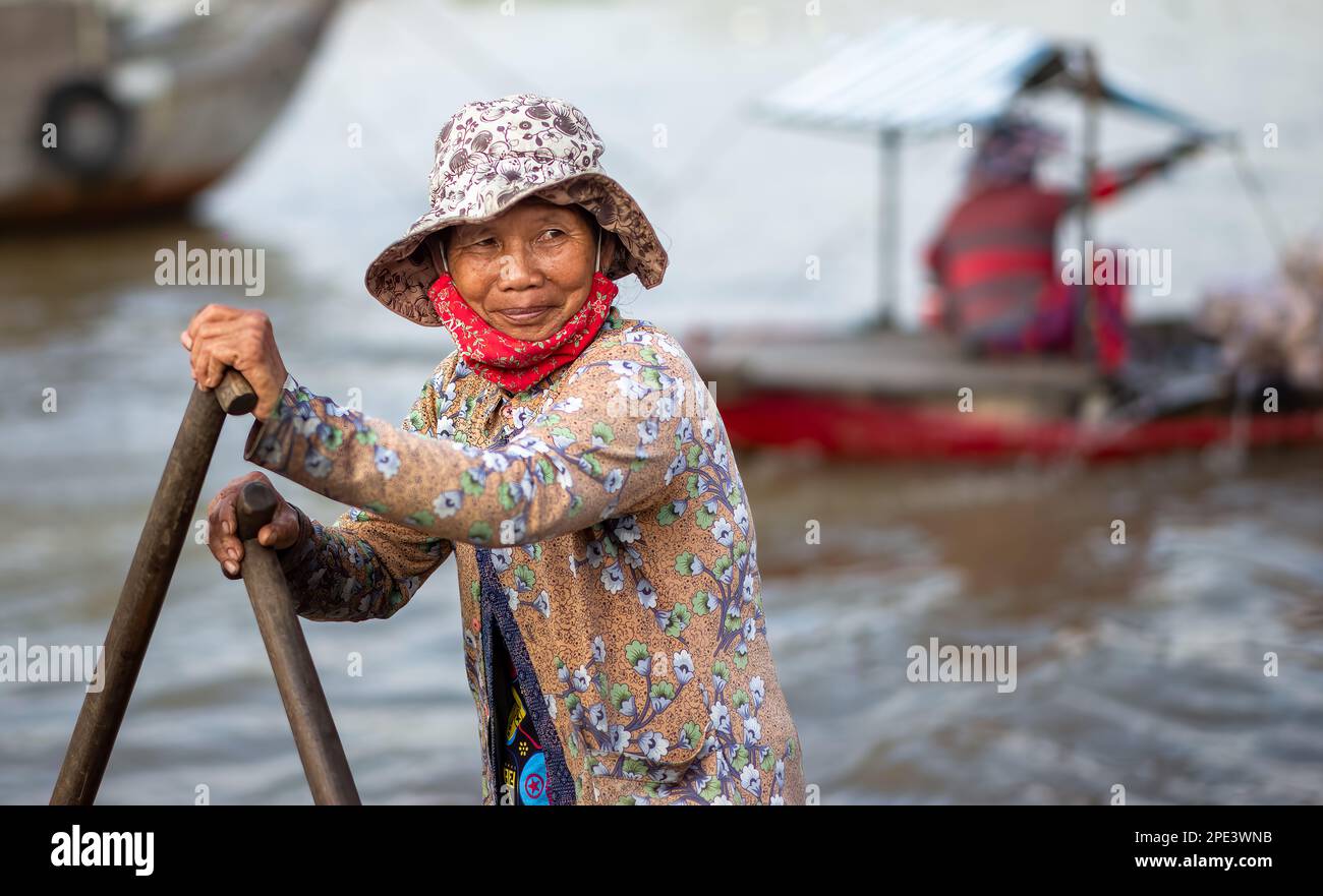 An elderly woman stands to row her boat on the Mekong River at Long ...
