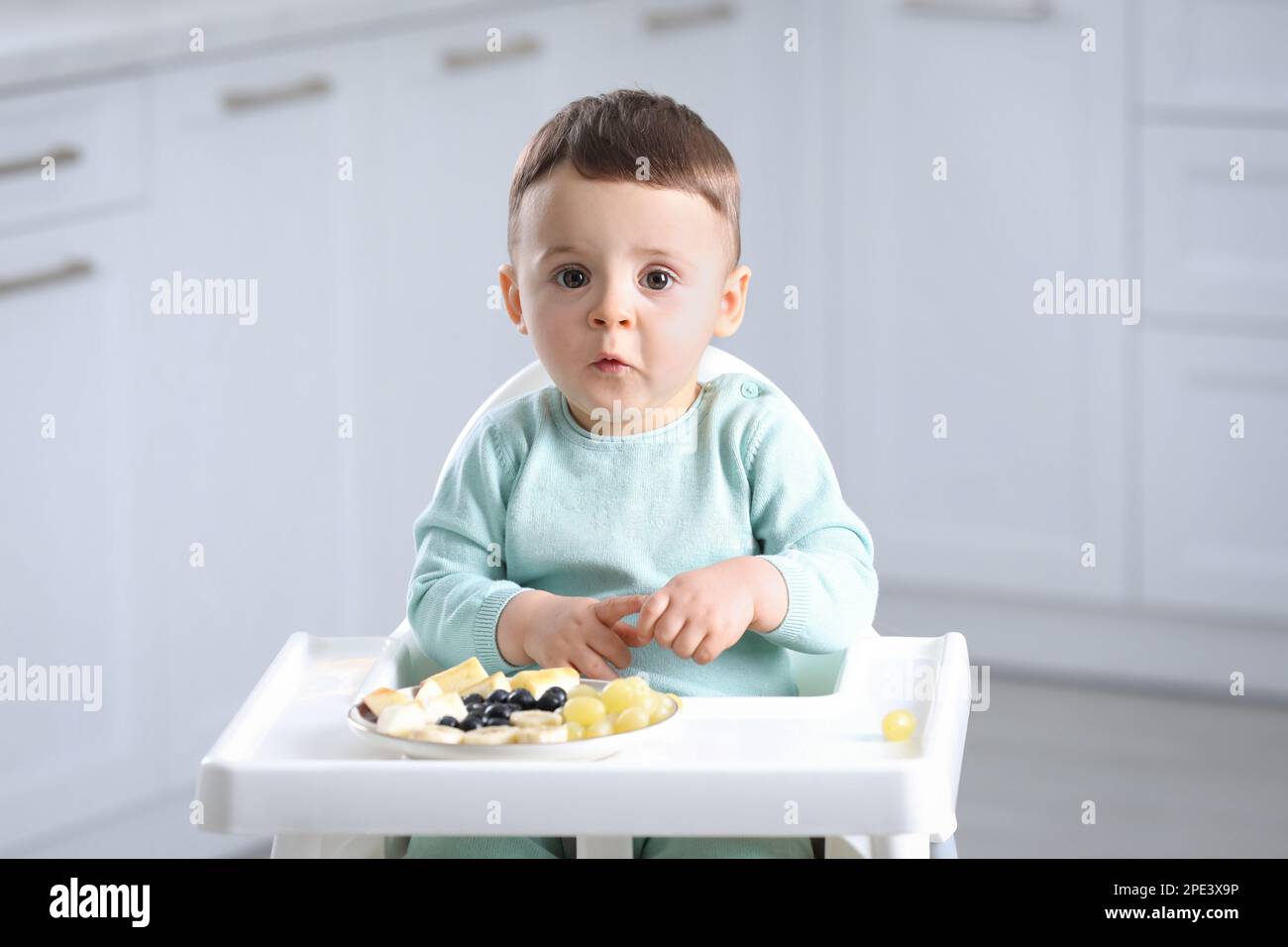 Cute little baby eating healthy food in high chair at home Stock Photo ...