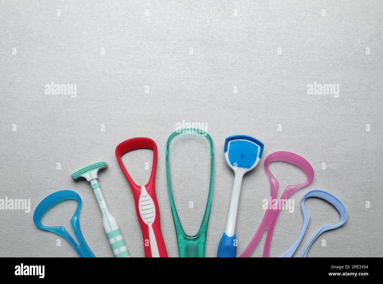 Different tongue cleaners on light grey table, flat lay. Space for text ...