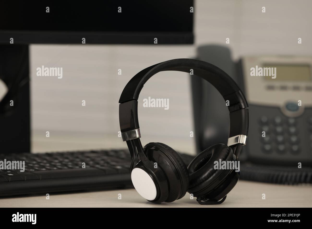 Modern headphones, desktop telephone and computer on table indoors ...