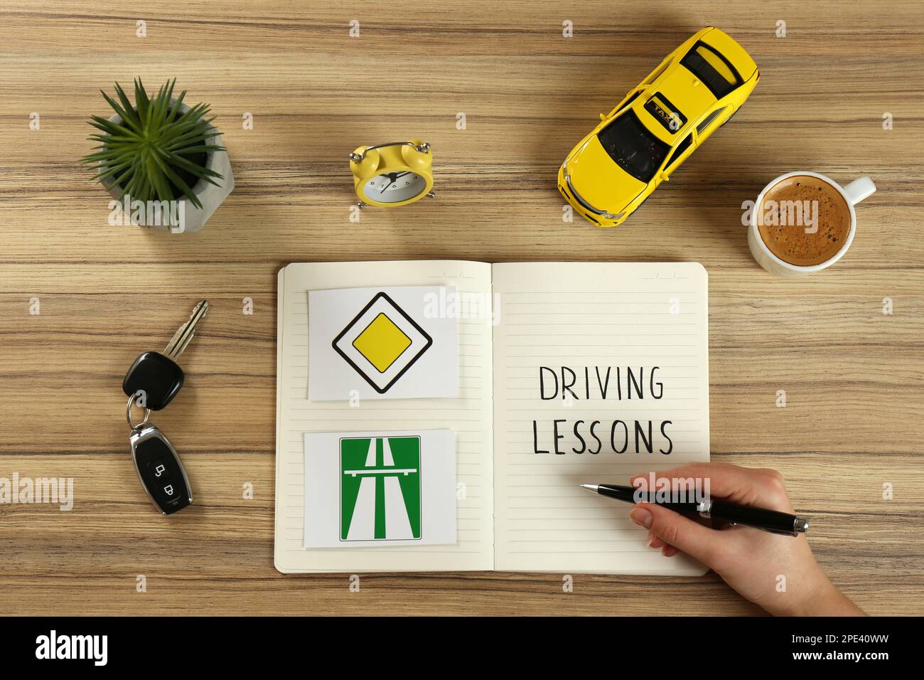 Woman with workbook for driving lessons and road signs at wooden table ...