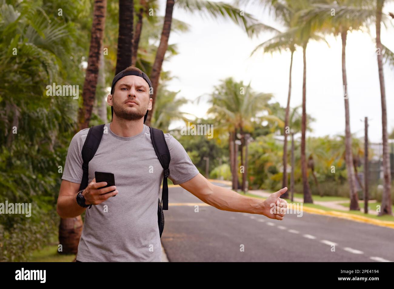 Young man traveling around tropical country, hailing a ride, catching a ...
