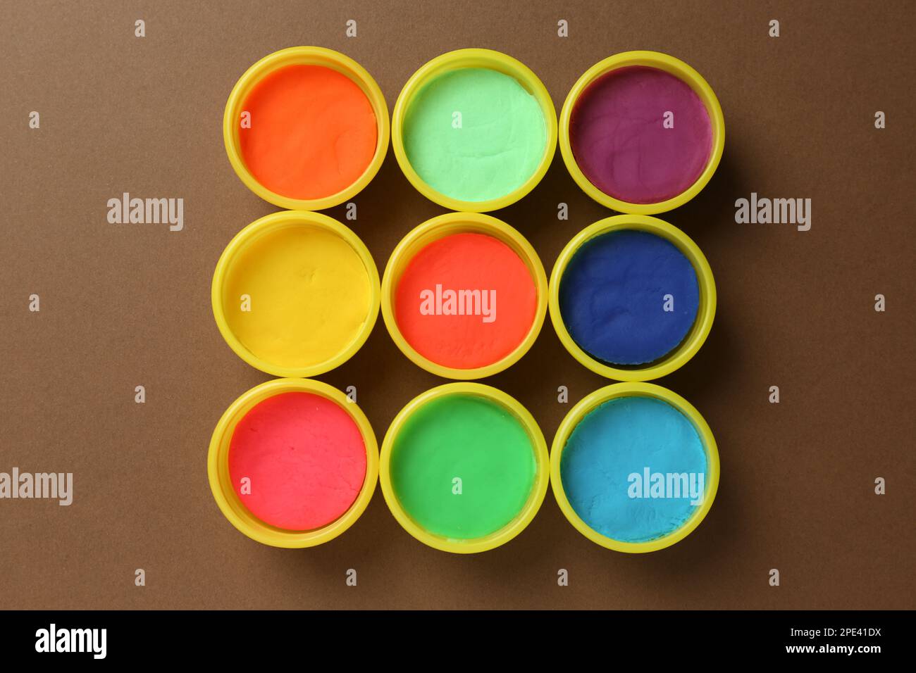 Plastic containers with colorful play dough on brown background, flat ...