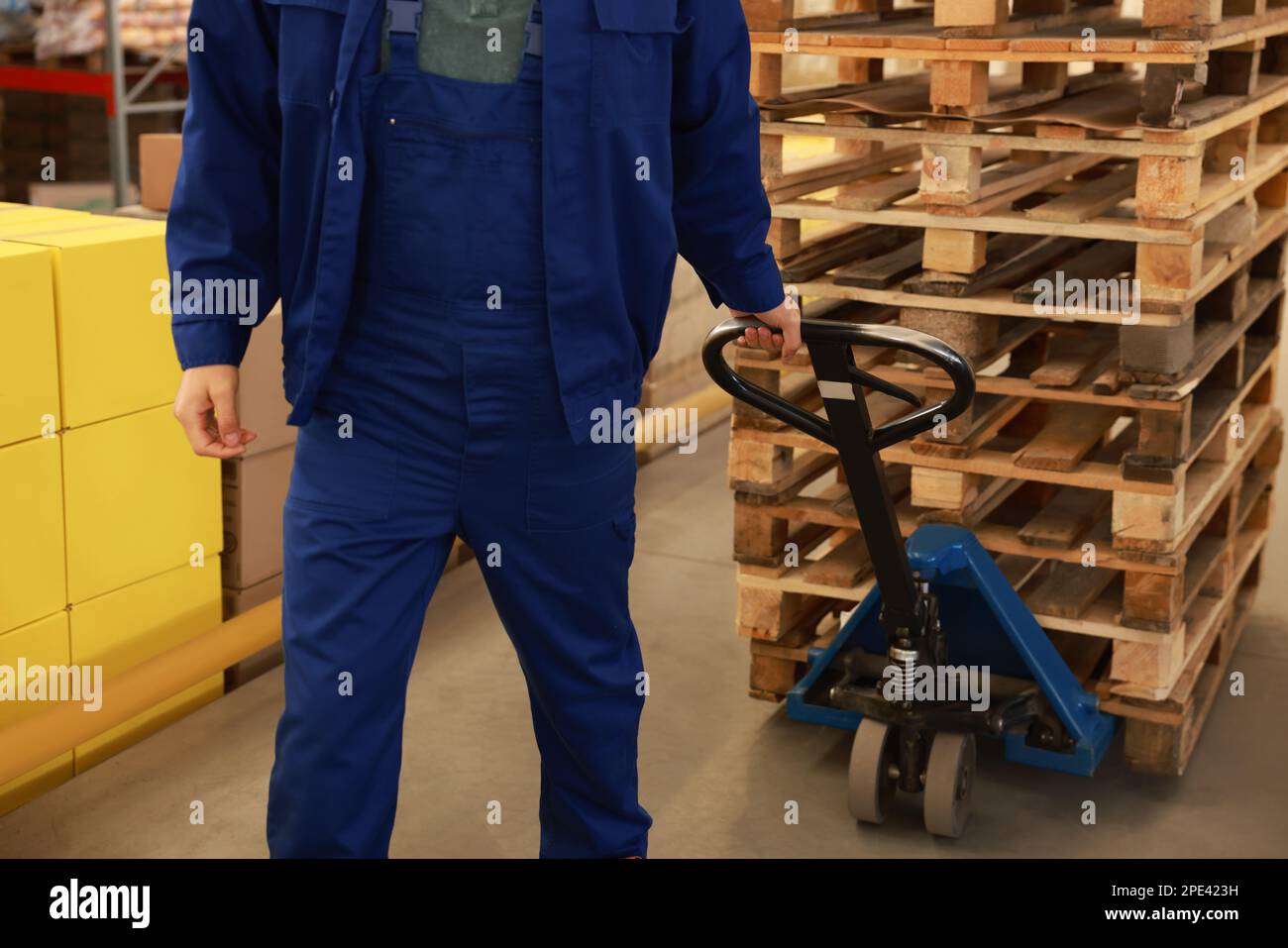 Worker moving wooden pallets with manual forklift in warehouse, closeup ...