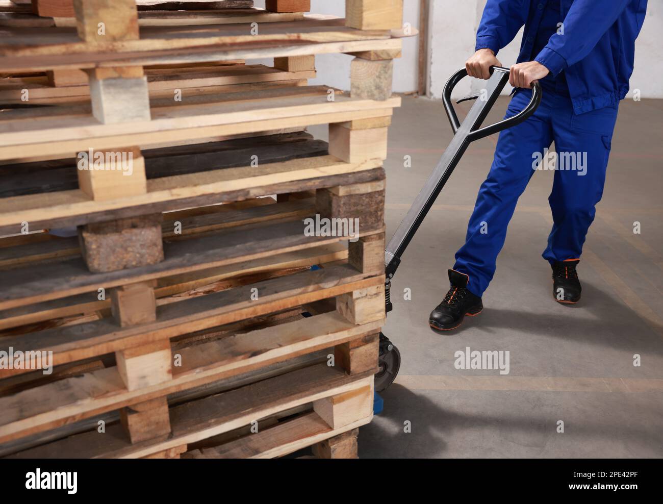 Worker moving wooden pallets with manual forklift in warehouse, closeup ...