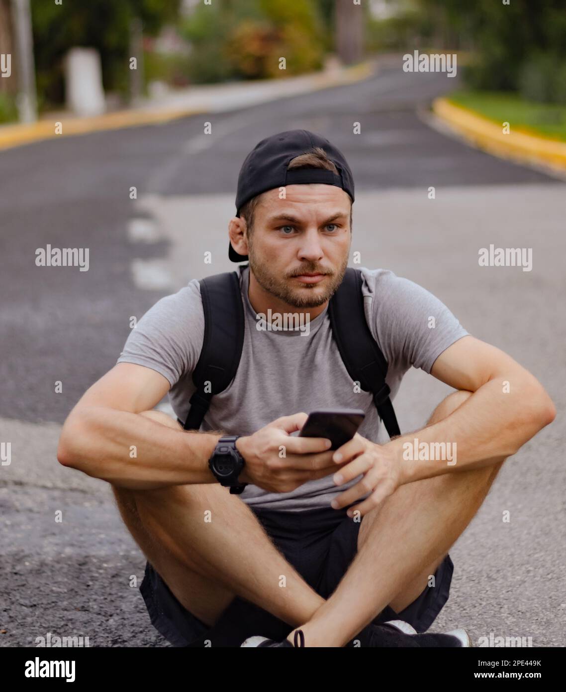 Man in cap with backpack sitting on the asphalt road in countryside ...