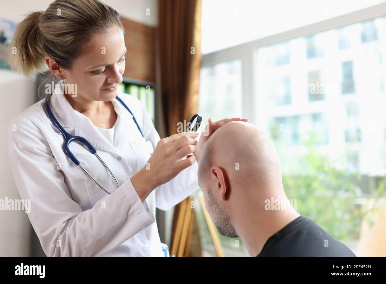 Friendly female doctor with magnifying glass looking at head skin of ...