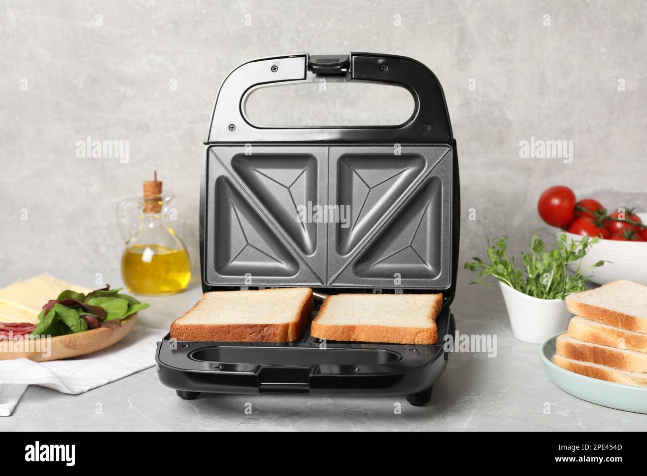 Modern sandwich maker with bread slices and different products on light ...