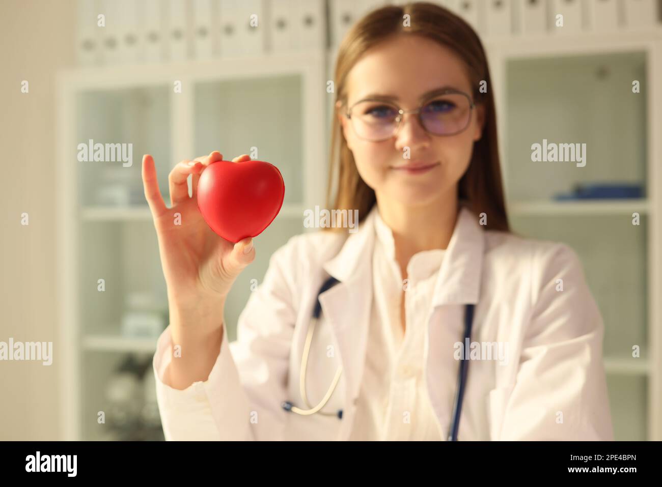 Young female cardiologist with stethoscope holds red heart in her hand ...