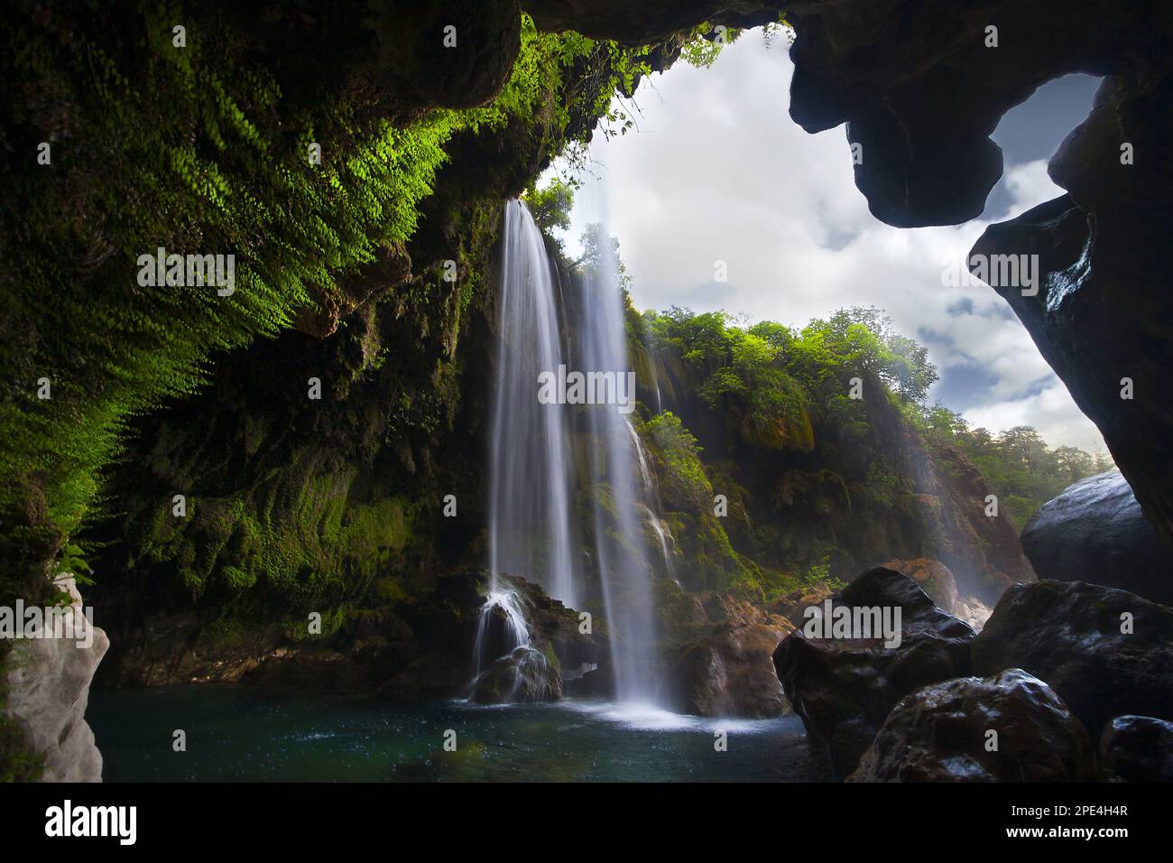A majestic waterfall cascades down a steep rocky embankment, creating a ...