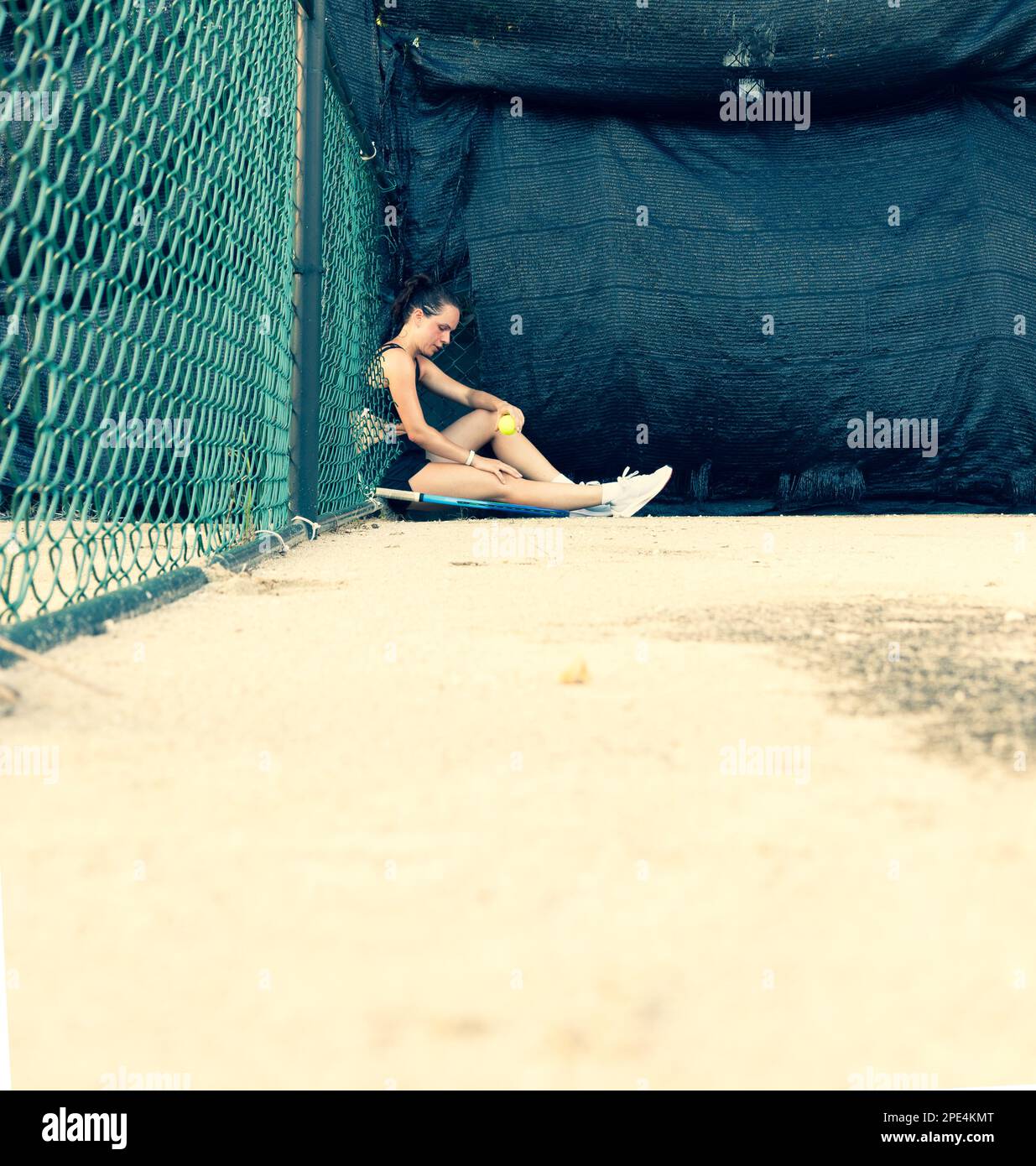 A sad and tired female tennis player sits on the ground of a tennis ...